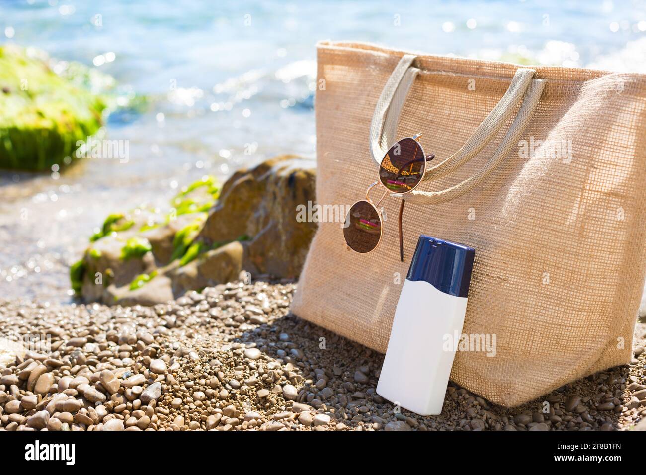 Beach bag with a white eco-friendly tube of sunscreen on a pebble coast ...