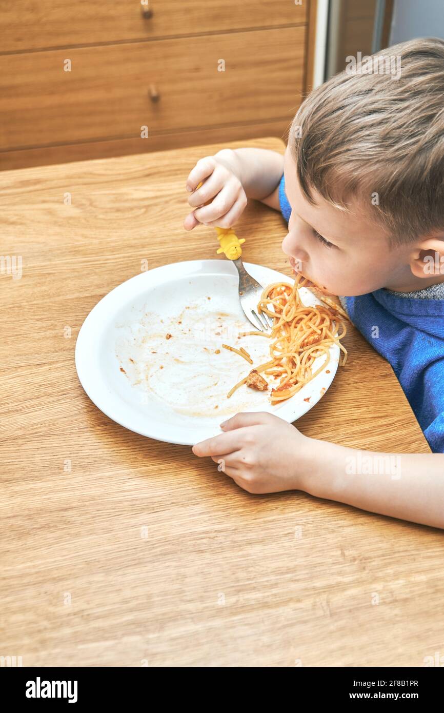 Lovely boy kid with large eyes eats sloppy delicious pasta with yellow ...