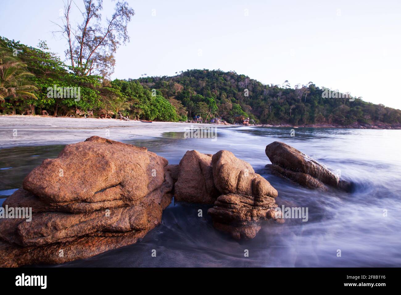 Ancient rocks stones on the tropical beach at dusk. Soft ocean waves ...