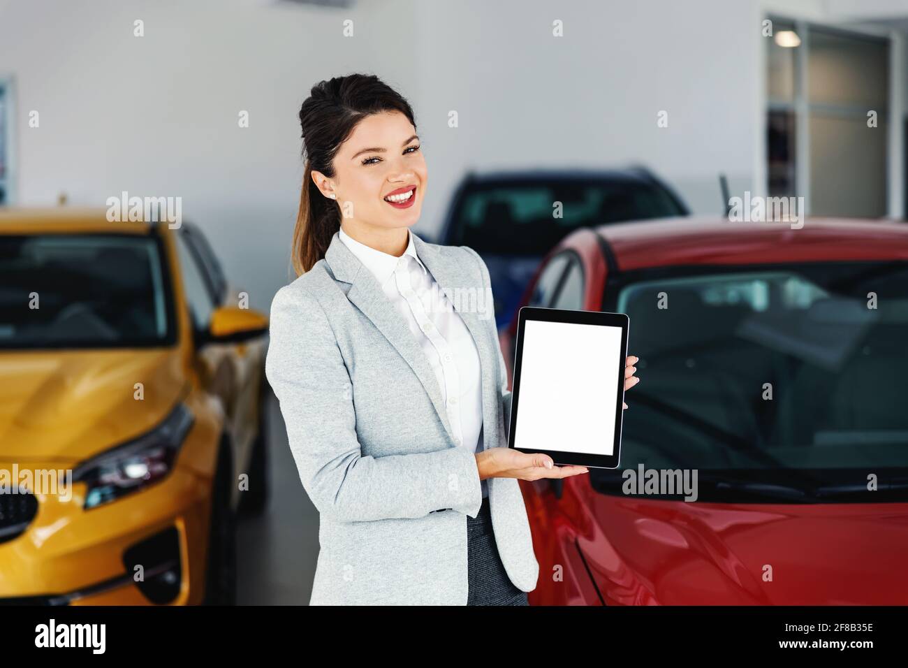 Friendly, smiling female car dealer standing in car salon and showing ...