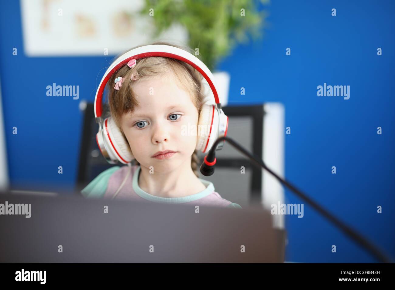 Little girl in headphones sits in front of monitor with microphone ...