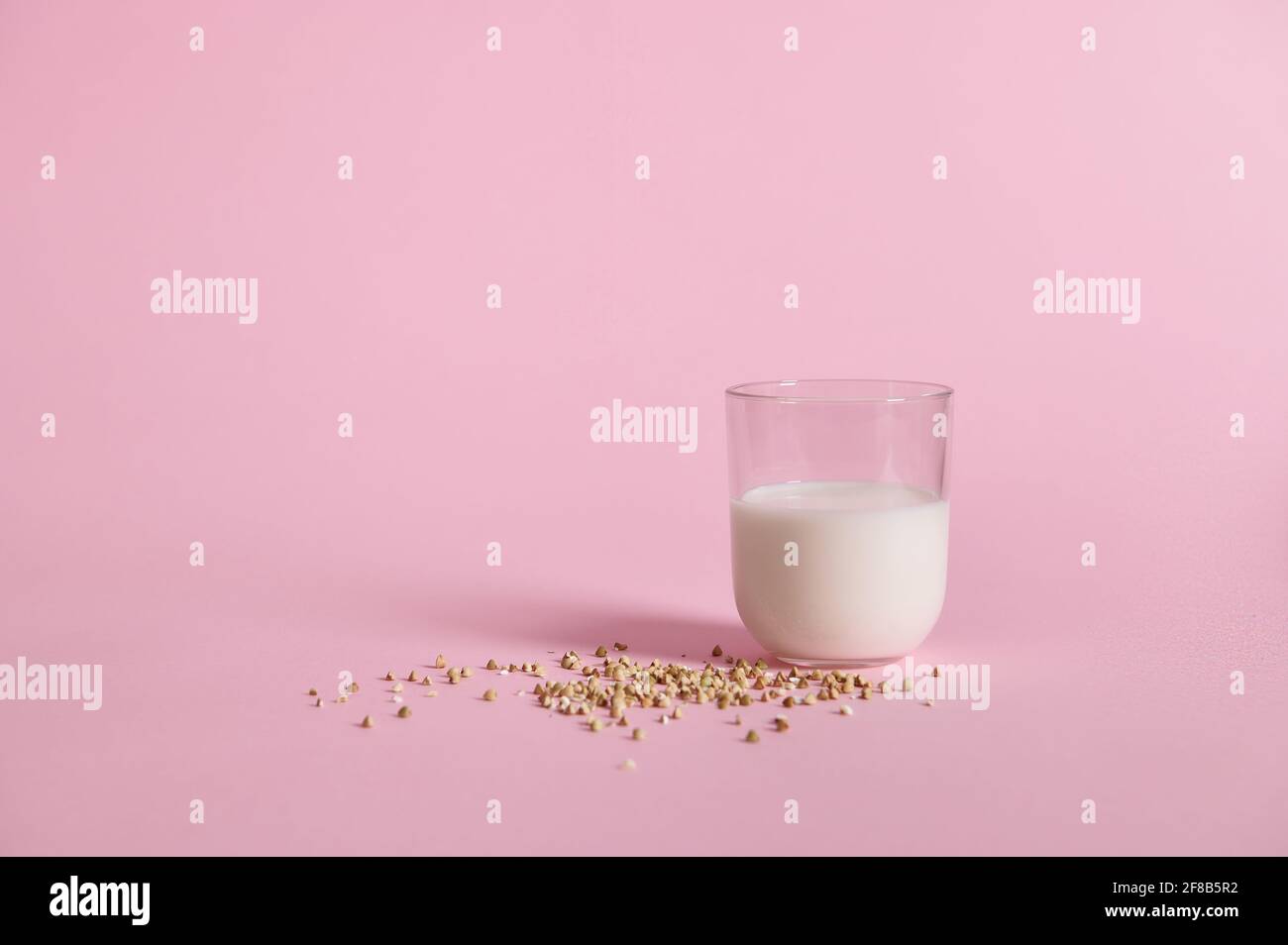 Raw buckwheat seeds and glass with milk on pink background. Closeup ...