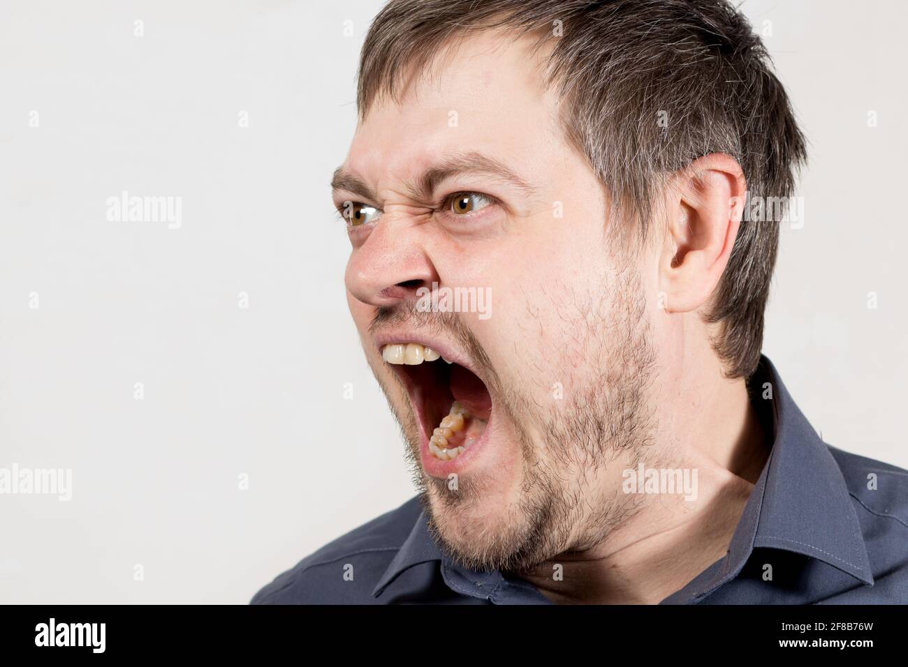 A furious angry man shouts open-mouthed on a white background to copy ...