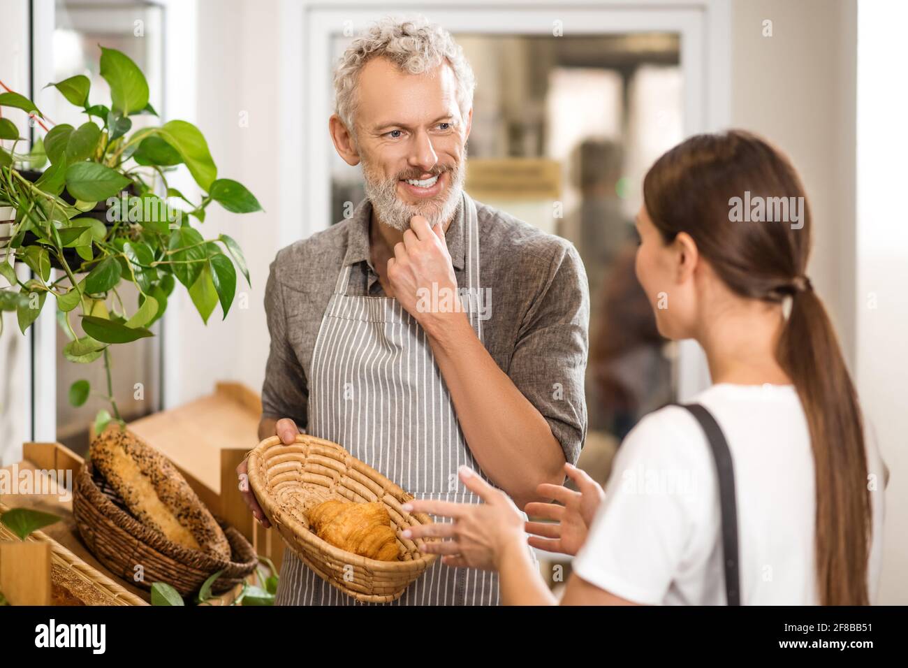 Man in apron showing croissant to customer Stock Photo - Alamy