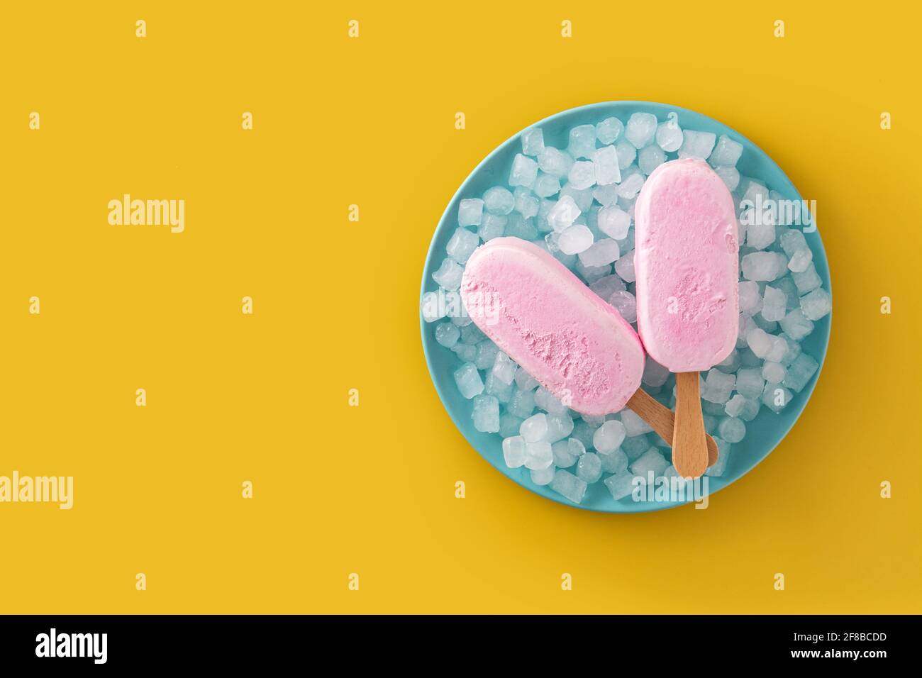 Strawberry popsicles and crushed ice on blue plate on yellow background ...