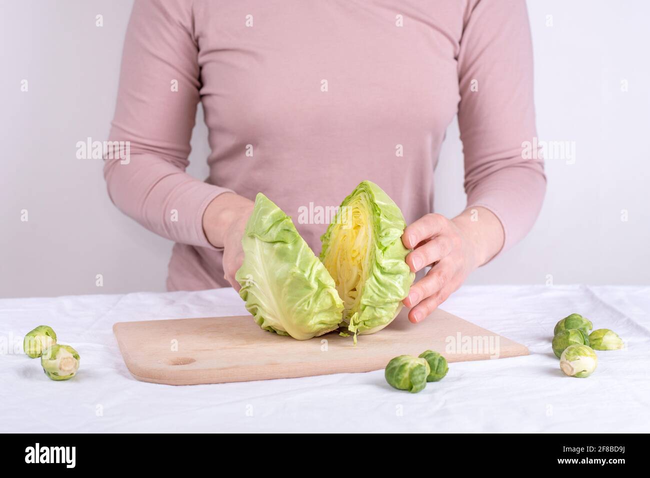 Female hands cutting into halves the head of a early cabbage on a white ...