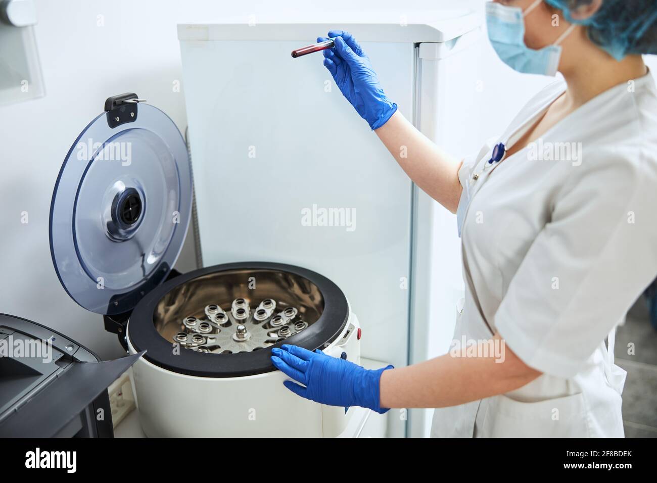 Biochemist with a vacutainer standing before the centrifuge machine ...