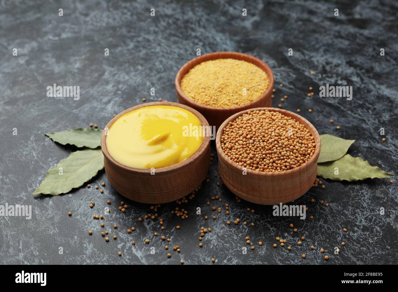 Bowls with mustard seeds, sauce and powder on black smoky background ...