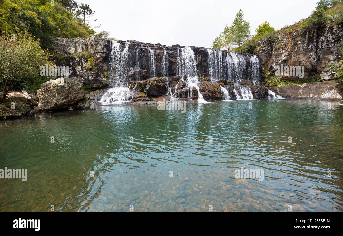 Beautiful waterfall with trees, rocks, and shiny lake at Cascade Barry ...