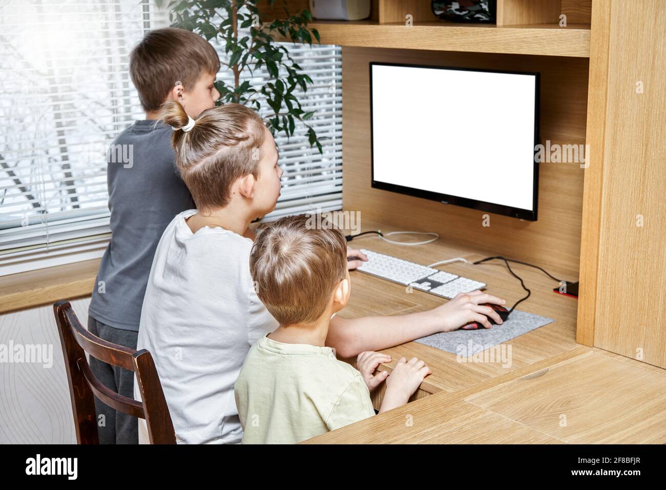 Delighted children sit on chair near brown wooden computer desk looking ...