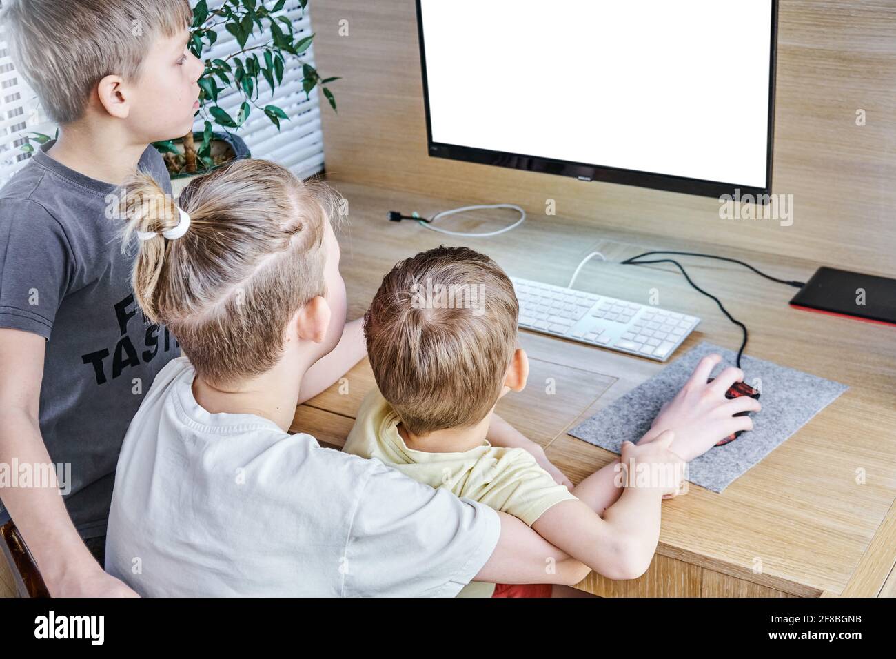 Schoolboy brothers sit at brown wooden desk and look into large ...