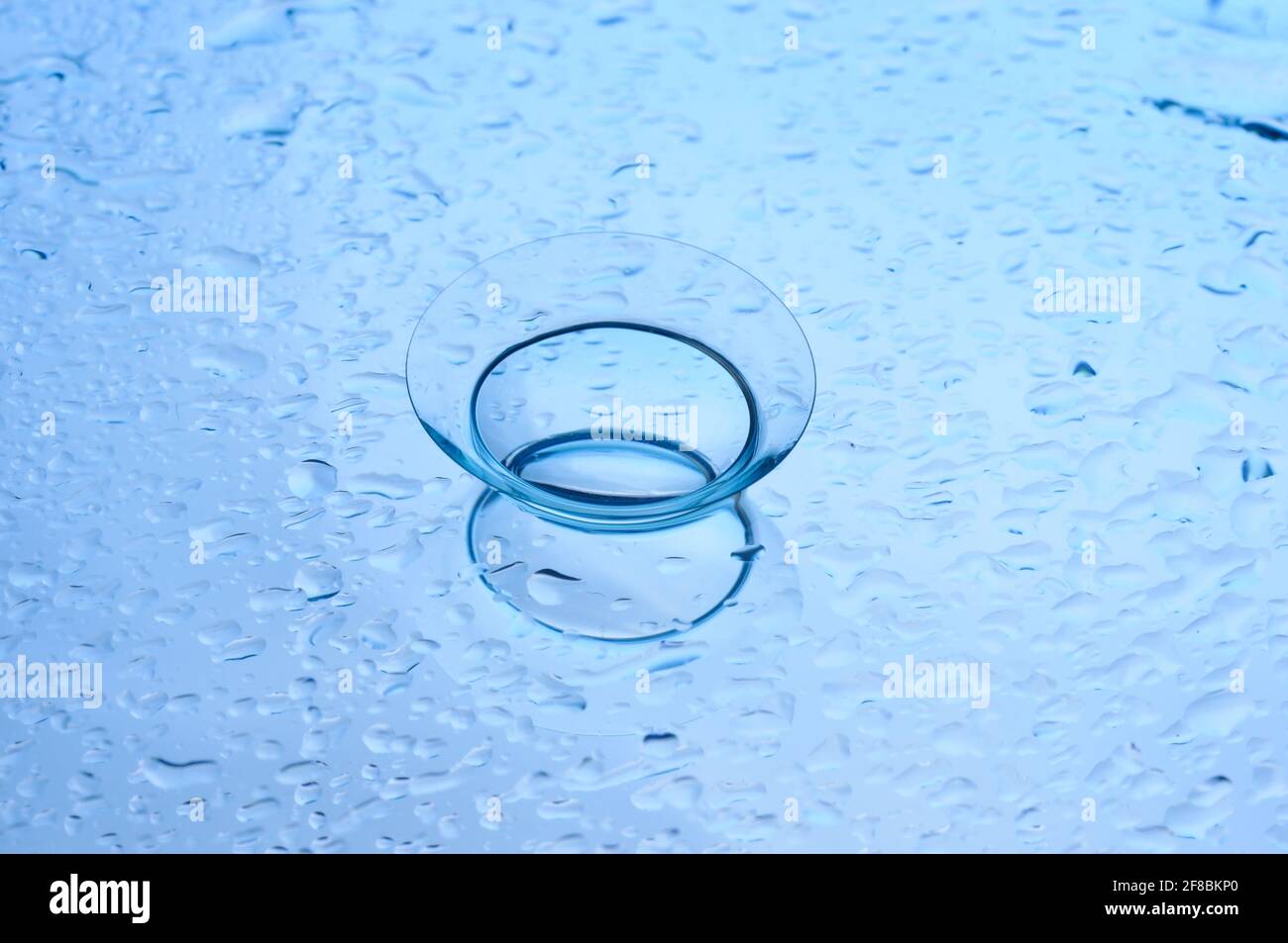 Contact lens with water drops on a mirror background. Blue toned image ...