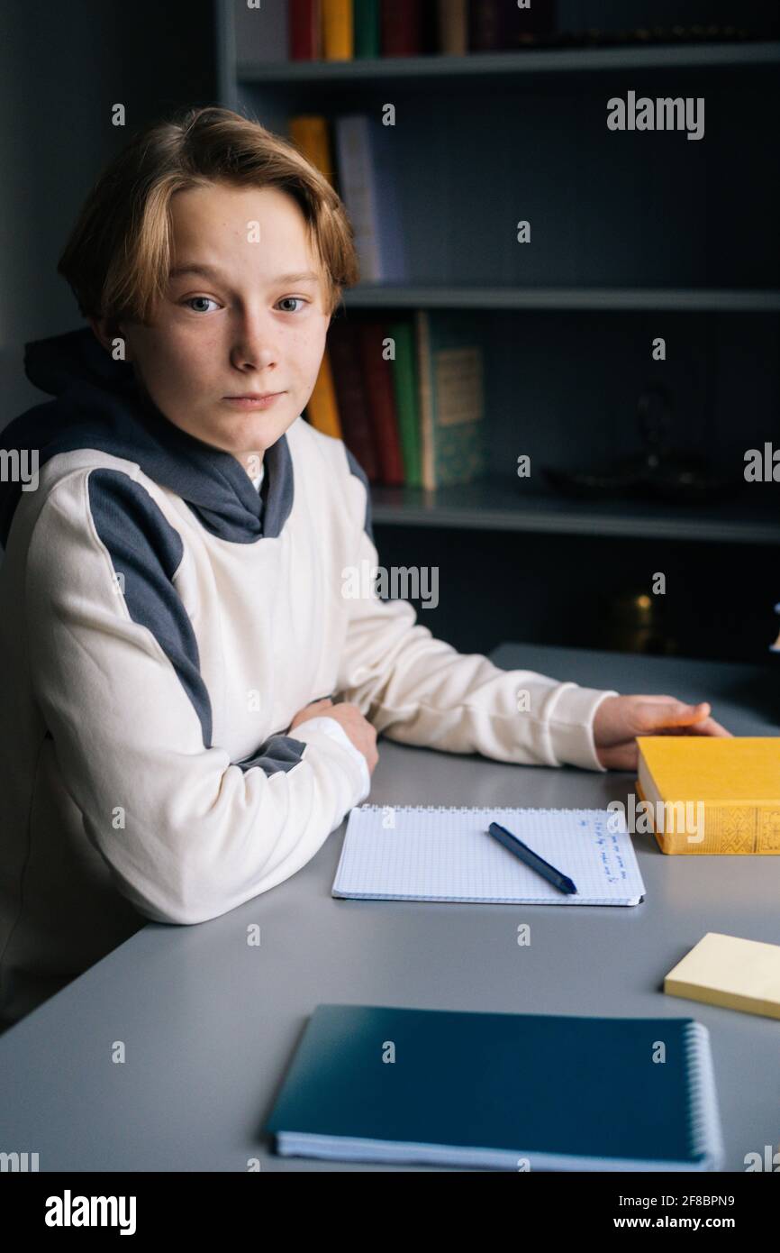 Close-up view of smiling pupil boy sitting at desk with paper workbook ...