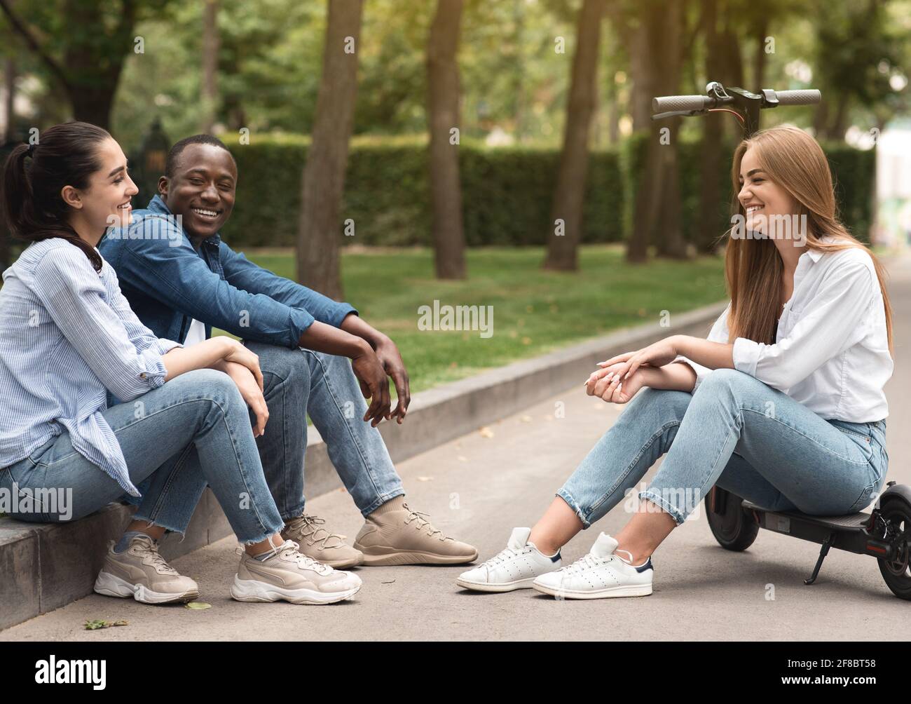 Three diverse friends spending time in park and talking Stock Photo - Alamy
