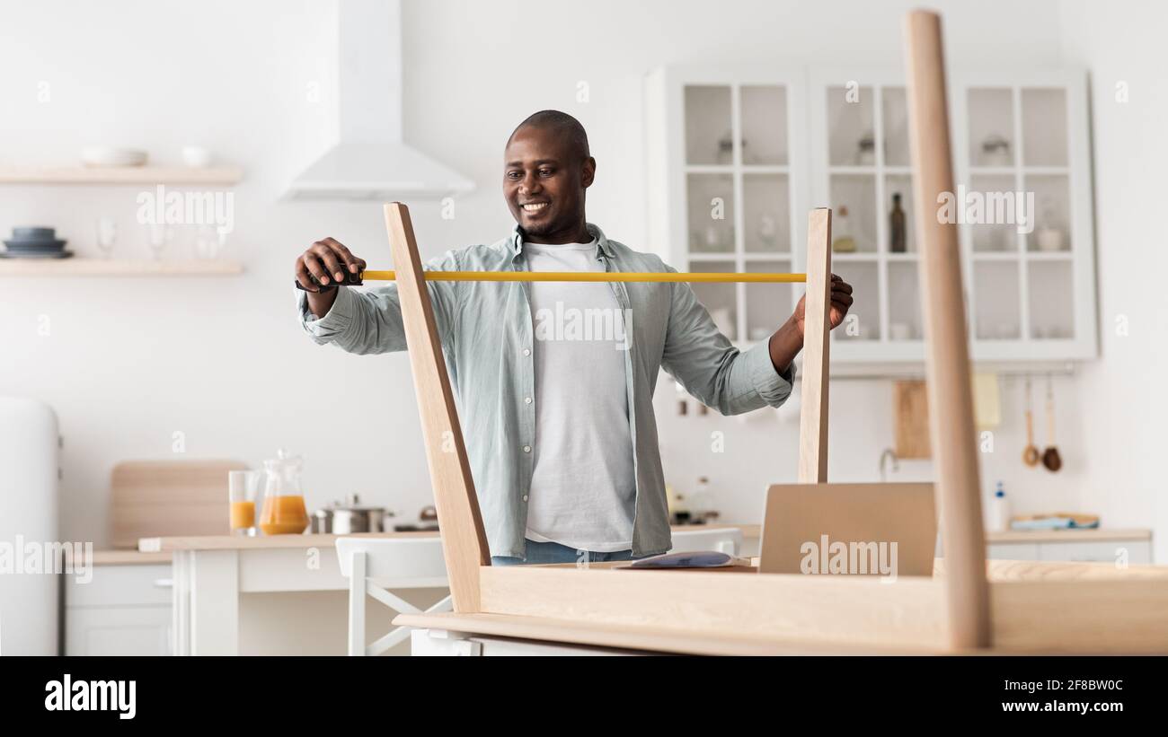 Excited black man measuring furniture with roulette, assembling new ...