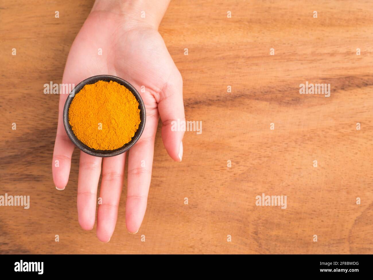 Turmeric powder in bowl between hands - Curcuma longa Stock Photo - Alamy