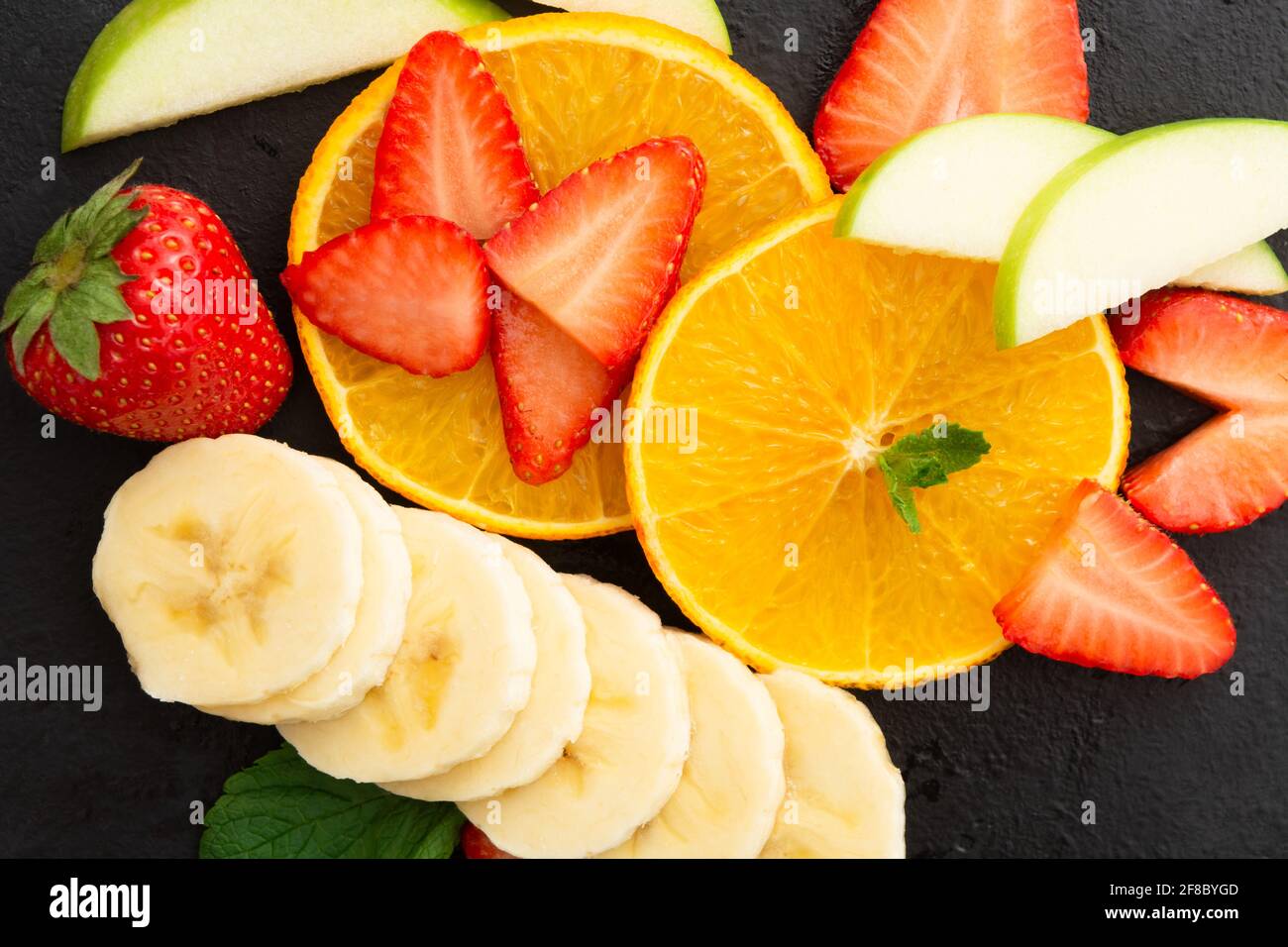 Closeup strawberry, banana, orange, apples and mint on dark stone table ...