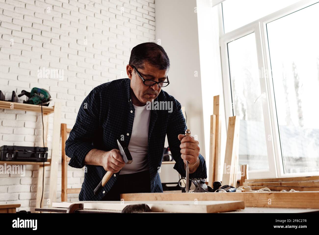Middle-aged man carpenter working in a workshop with chisel and hammer ...