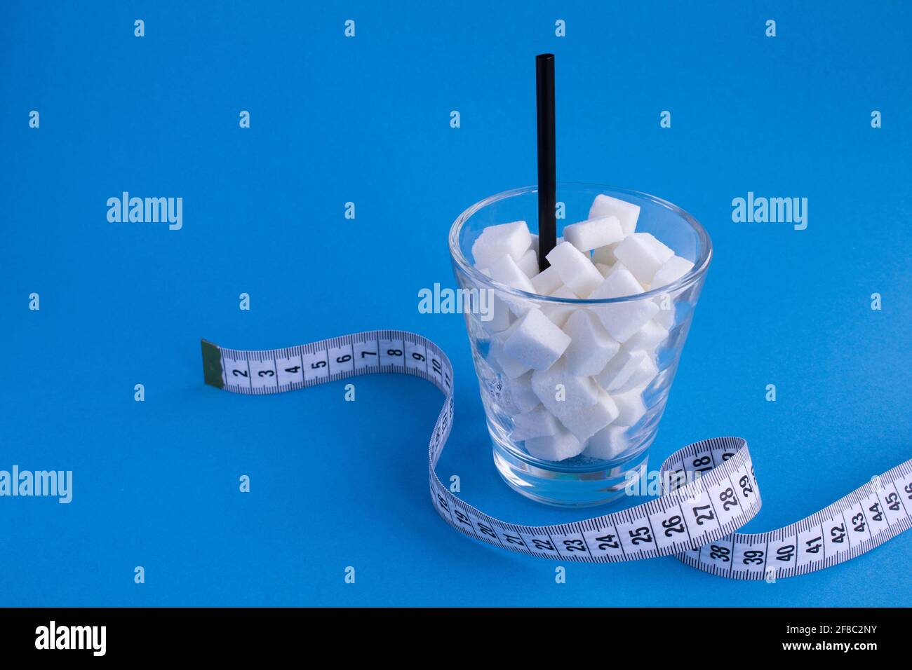 Glass with sugar cubes and white centimeter on the blue background.Copy ...