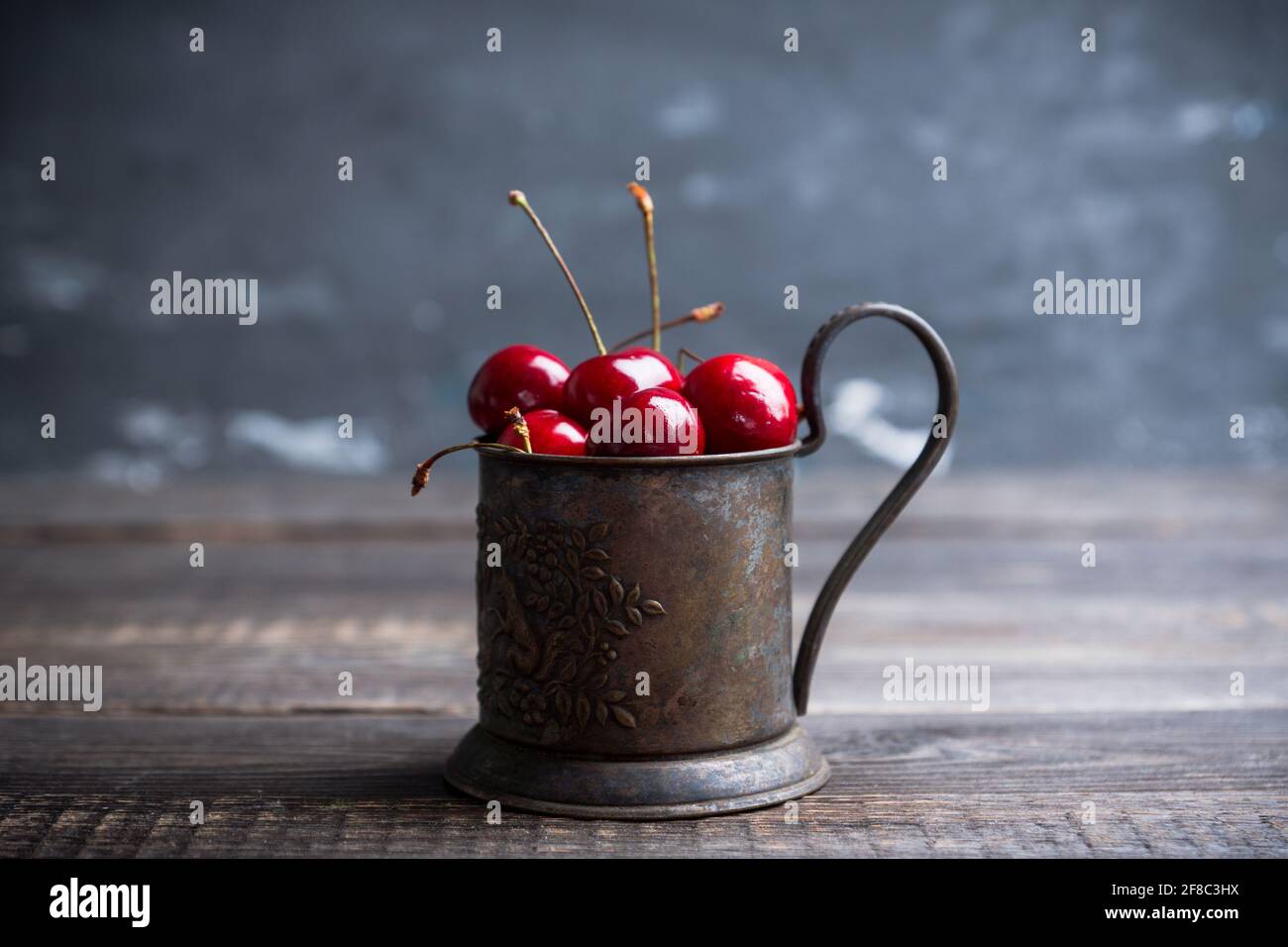Ripe and juicy cherries in old metal cup on the dark rustic background ...