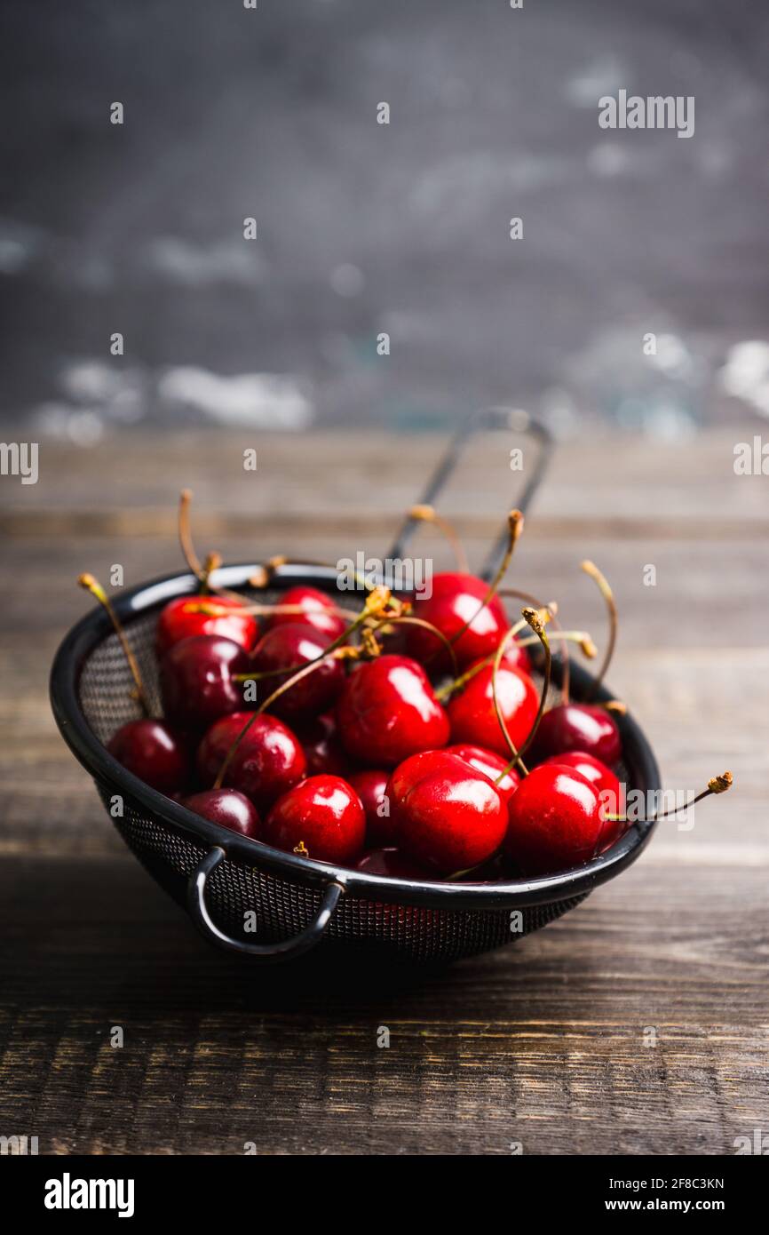 Ripe and juicy cherries in black metal strainer on the dark rustic ...