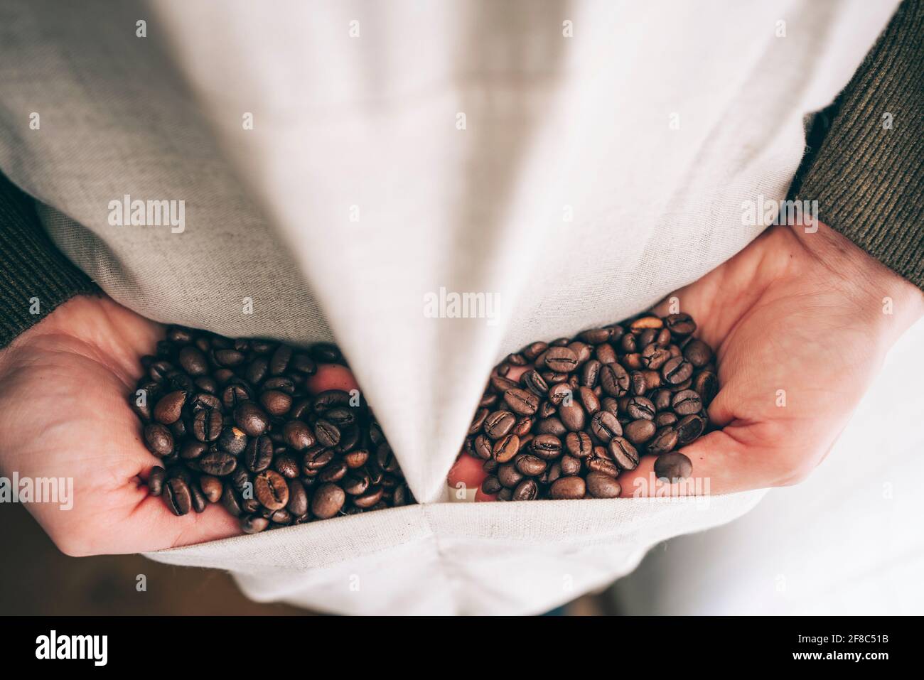 Two hands full of coffee beans sticking out of the pockets of a beige ...