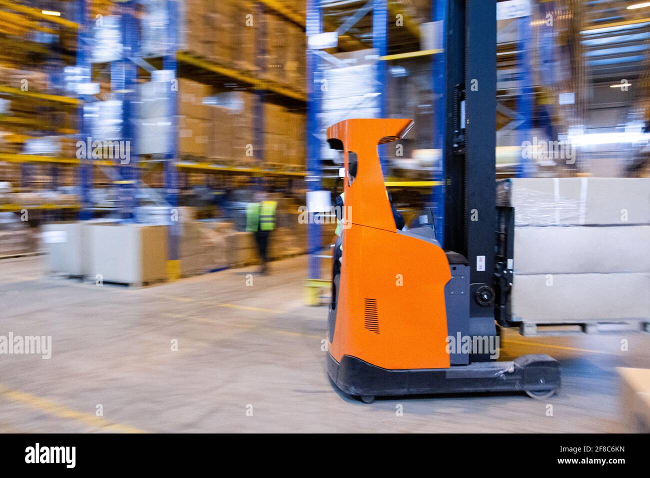 Warehouse worker driving a forklift truck full of goods between high ...
