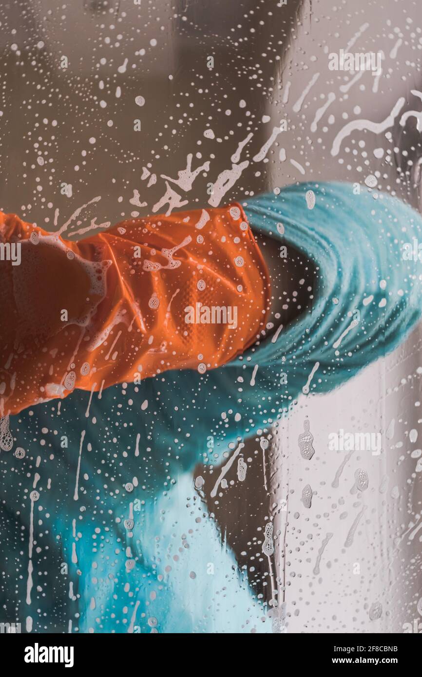Through the window pane, an orange rubber glove can be seen washing the ...