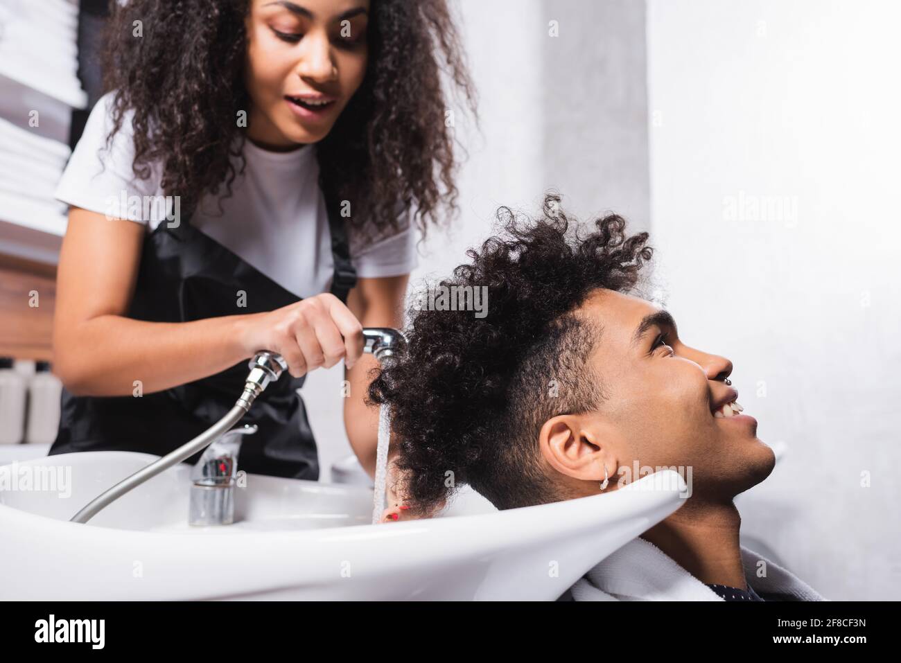 Positive african american client sitting near hairdresser with shower ...