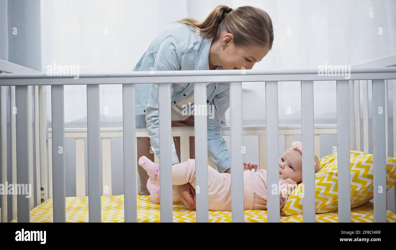 happy mother putting infant daughter in baby crib Stock Photo - Alamy