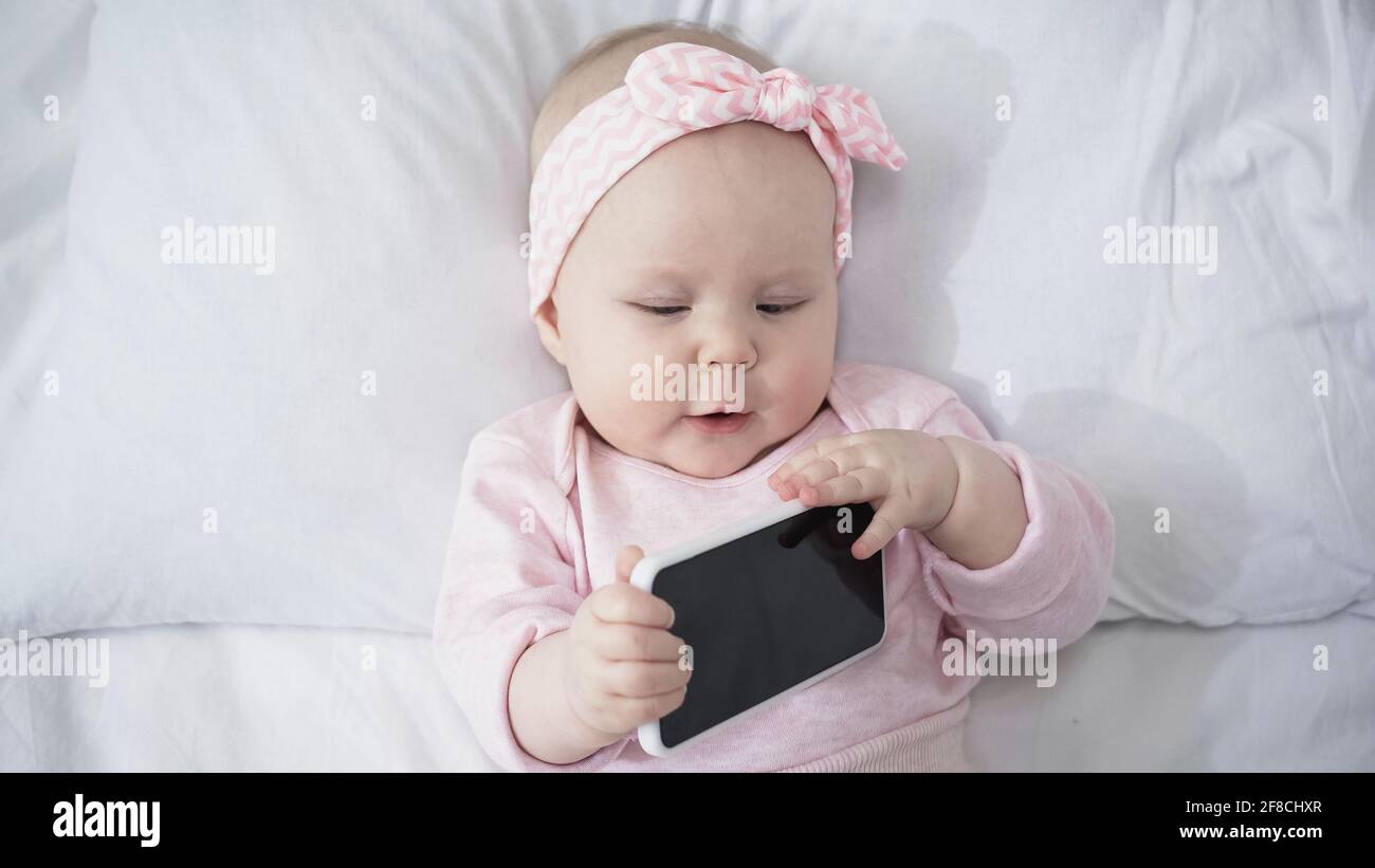 top view of infant baby holding smartphone with blank screen in bed ...