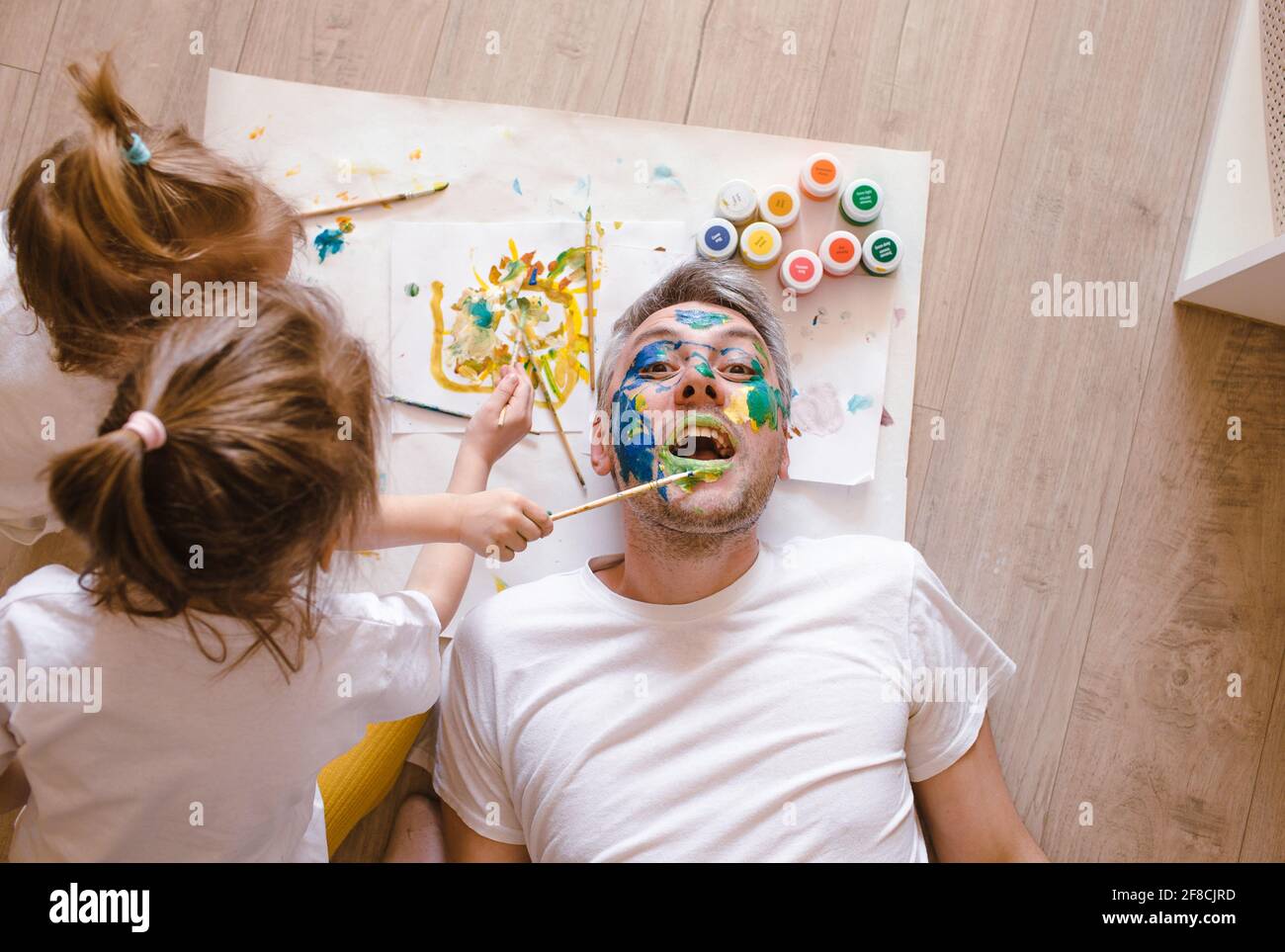 happy dad is lying on the floor, the children paint his face with ...