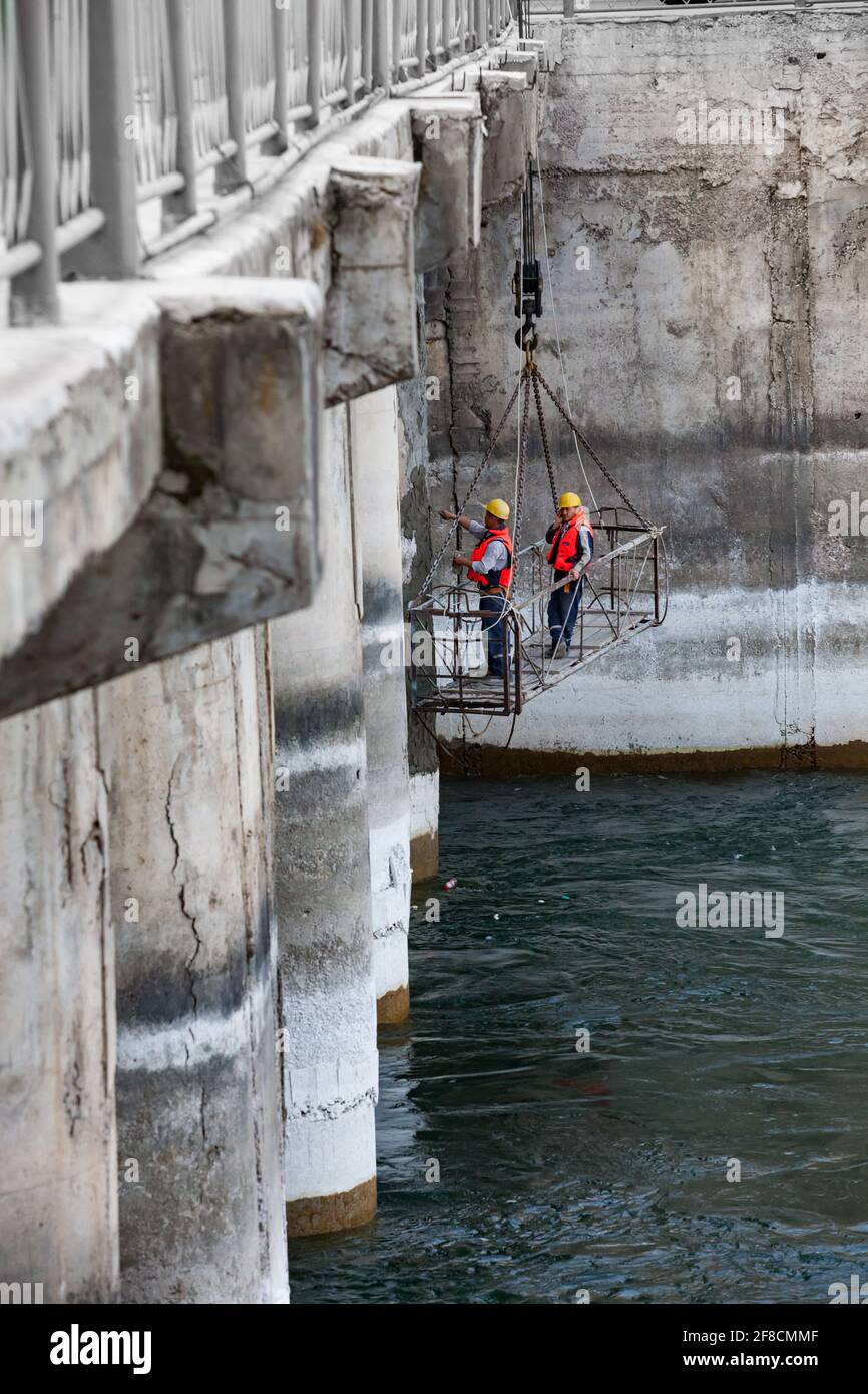Two maintenance engineers in suspended cradle watching Shardara river ...