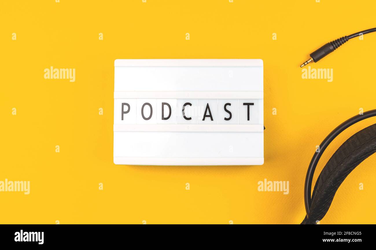 Podcast word on lightbox, yellow table background with headphones, top ...