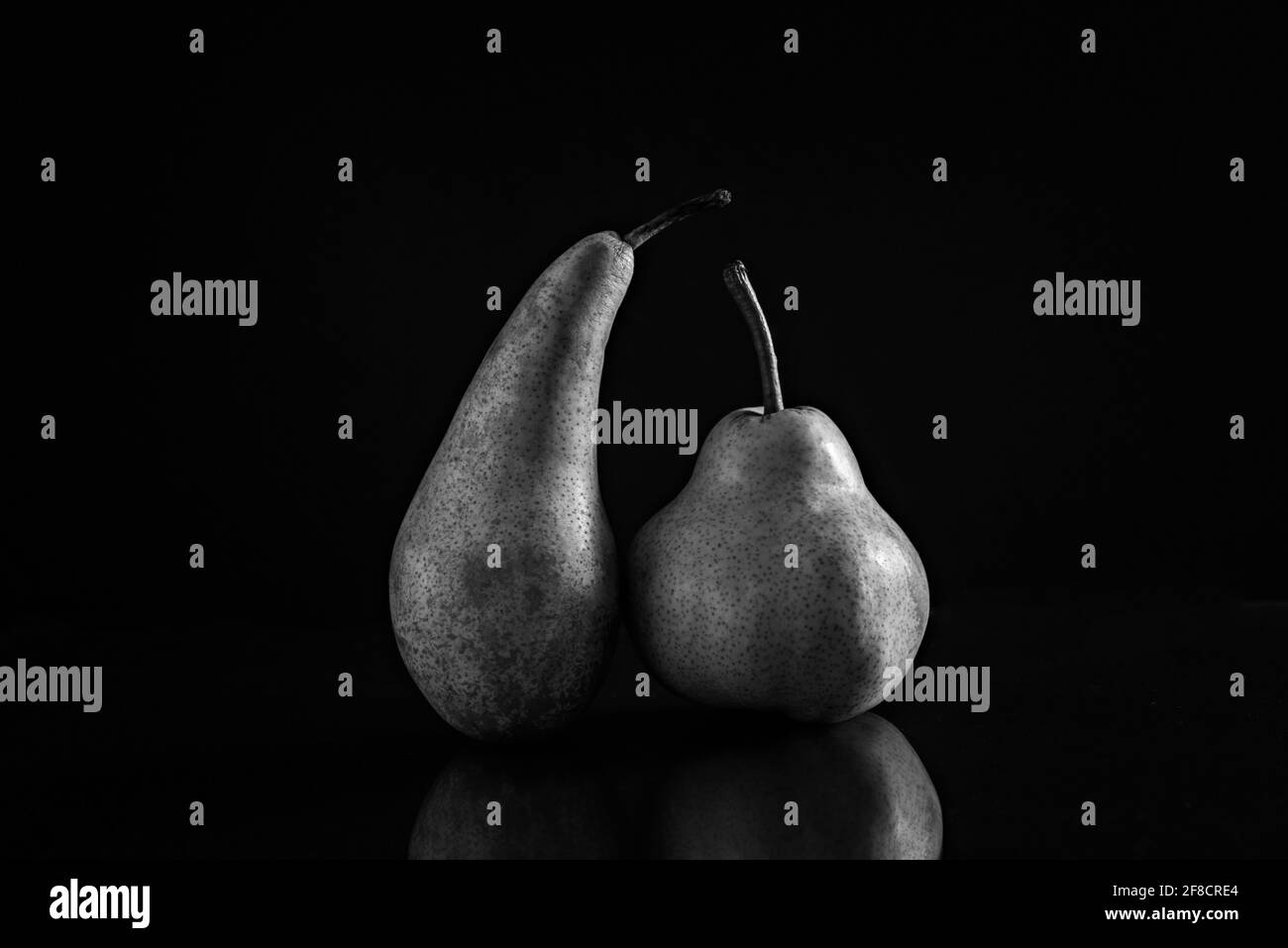 Two pears of different varieties on a black matte background. The ...