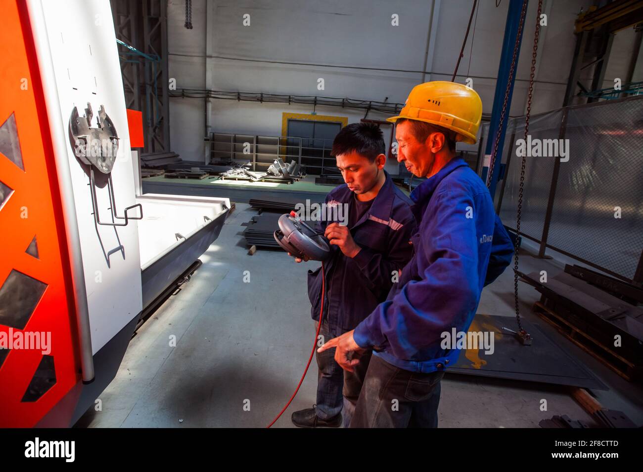 Locomotive-building plant. Two Asian workers programming CNC machine ...