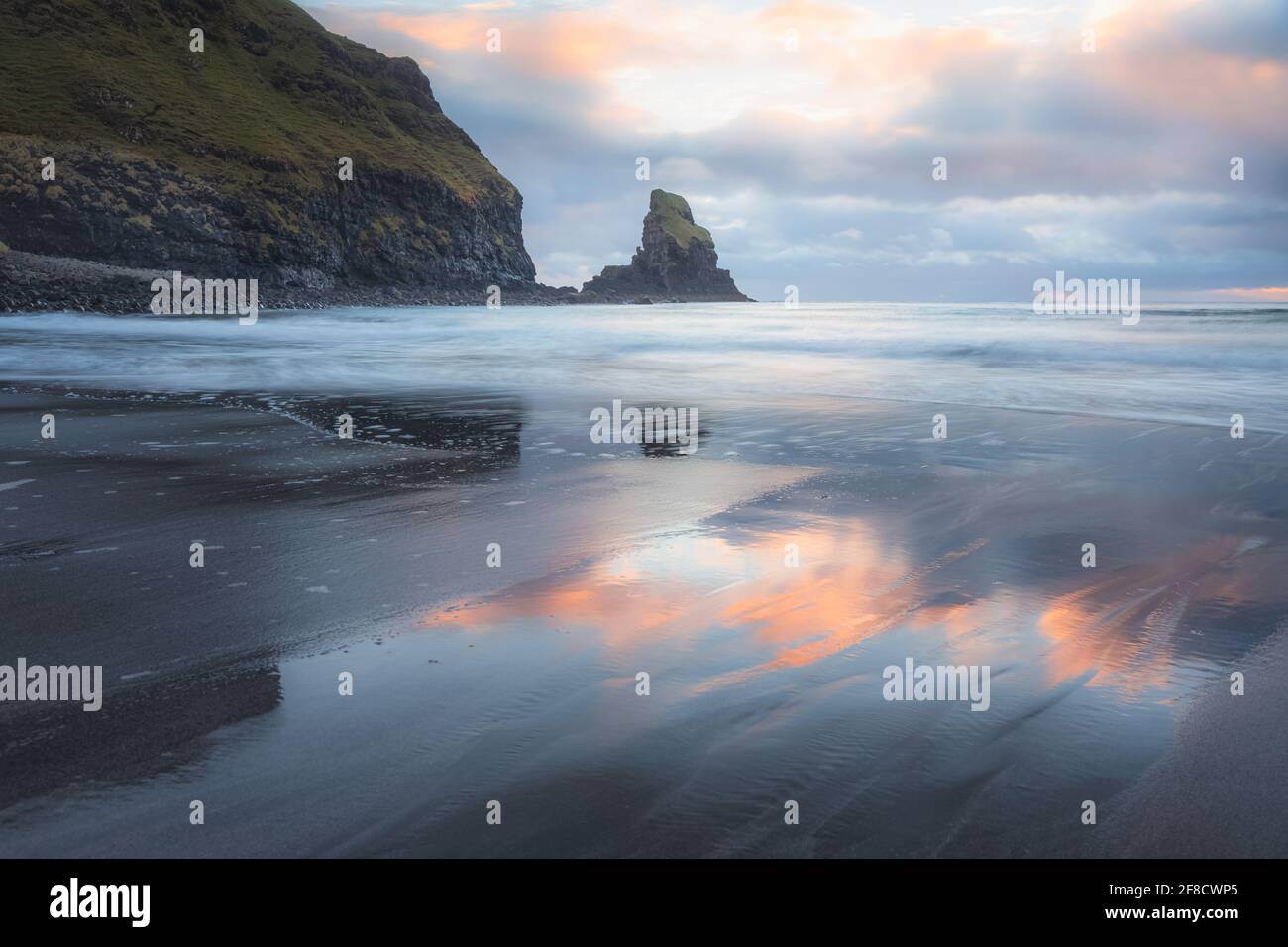 Idyllic seascape and sea stack with wet sand reflection during sunrise ...