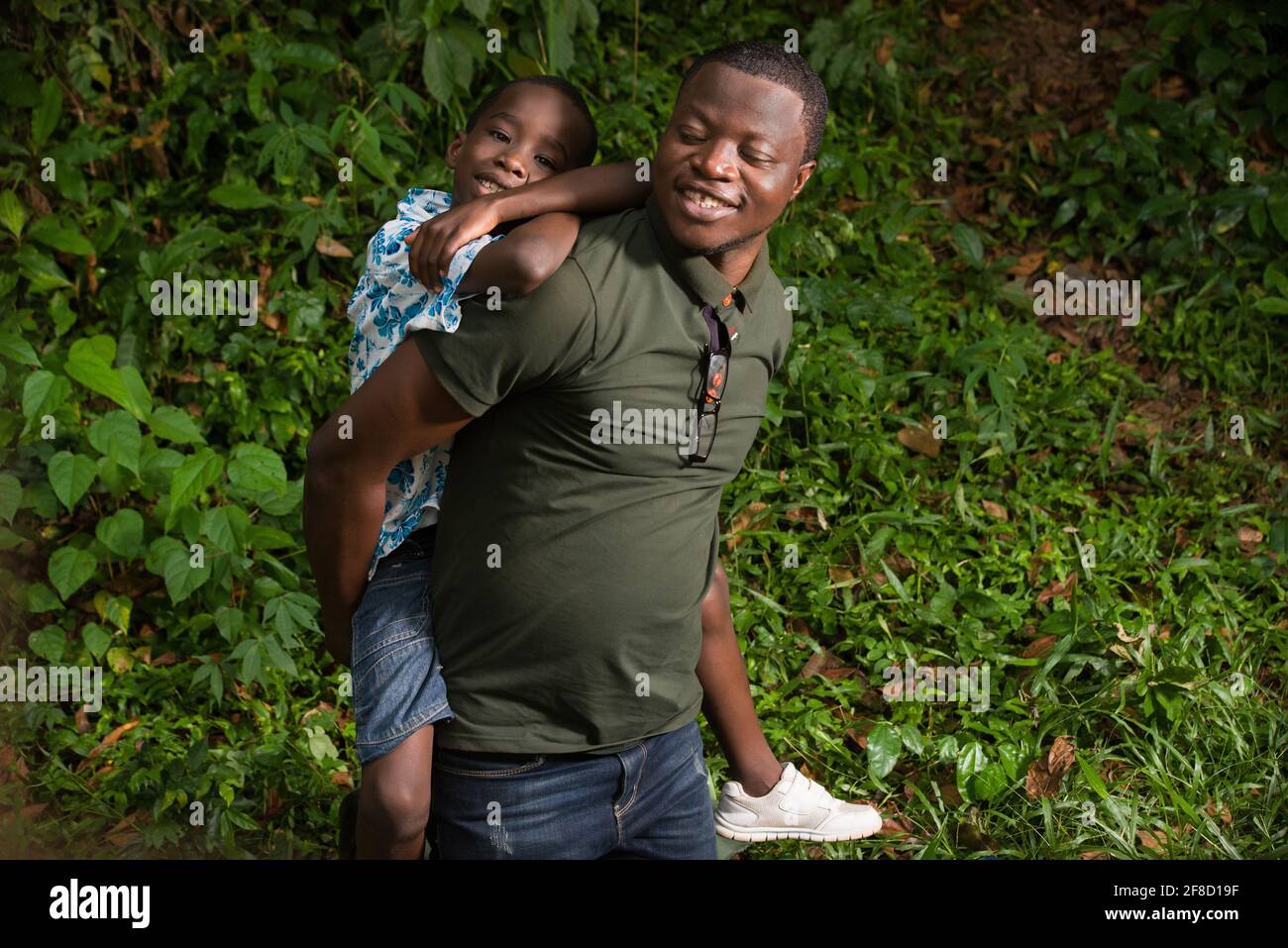 a young man kneeling in a park with his child on his back smiling Stock ...