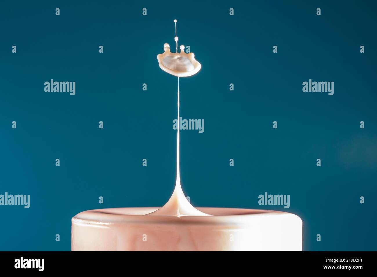 Two drops of milk fall into the long drink glass hitting each other ...