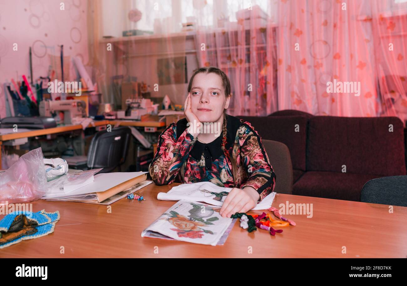 a disabled girl with slanted eyes sits at a table and smiles. People ...