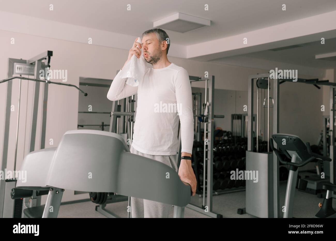 a tired man on a treadmill wipes sweat from his face with a towel ...
