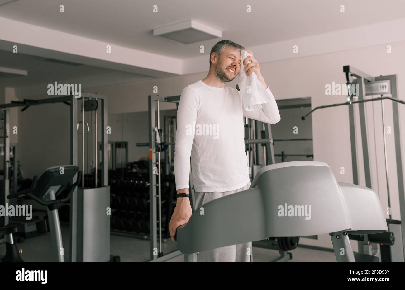 a tired man on a treadmill wipes sweat from his face with a towel ...