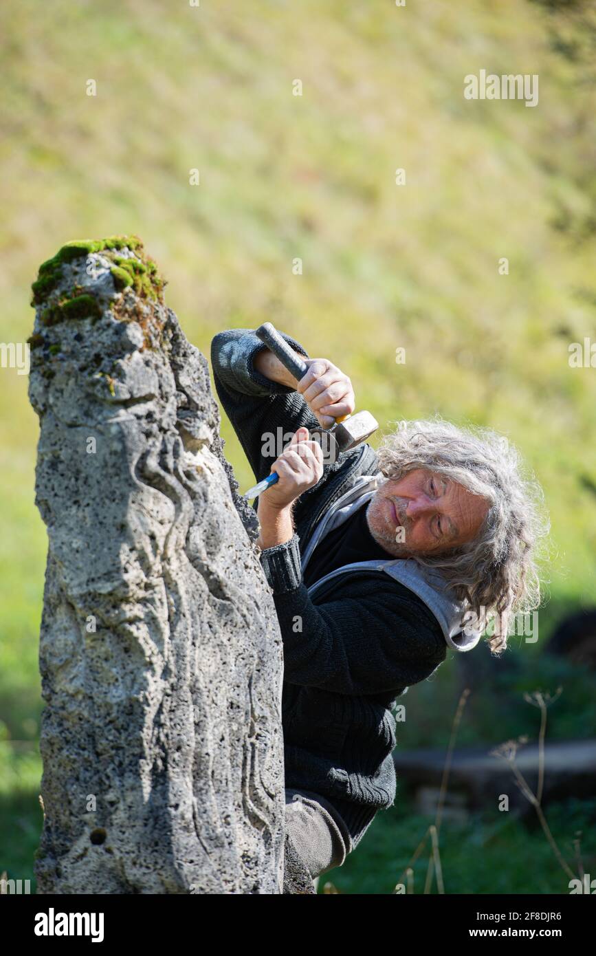 Precise devoted senior artist carving in stone with mallet and a chisel ...