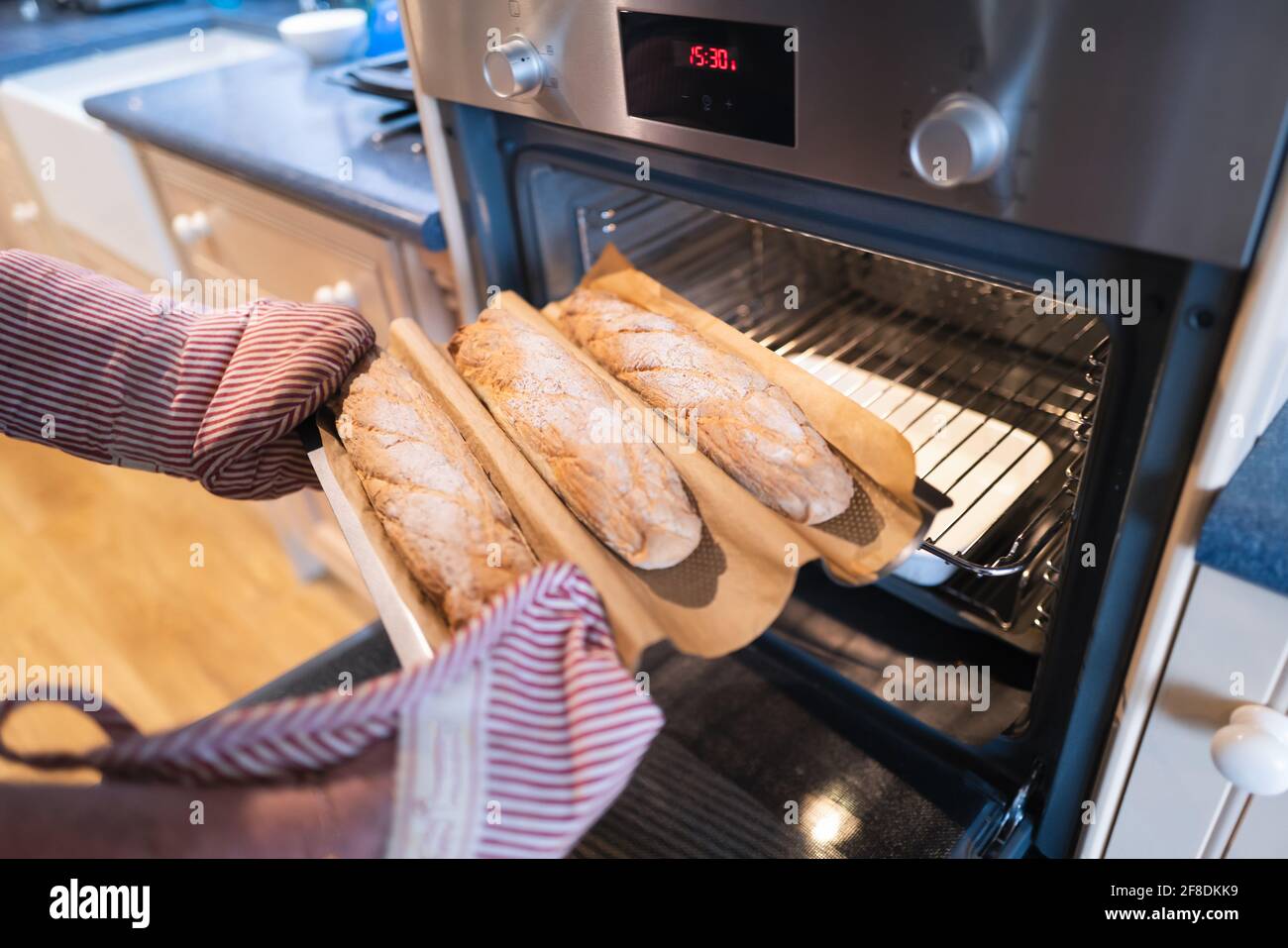 Freshly made baguettes being taken out of an oven with oven gloves. A ...