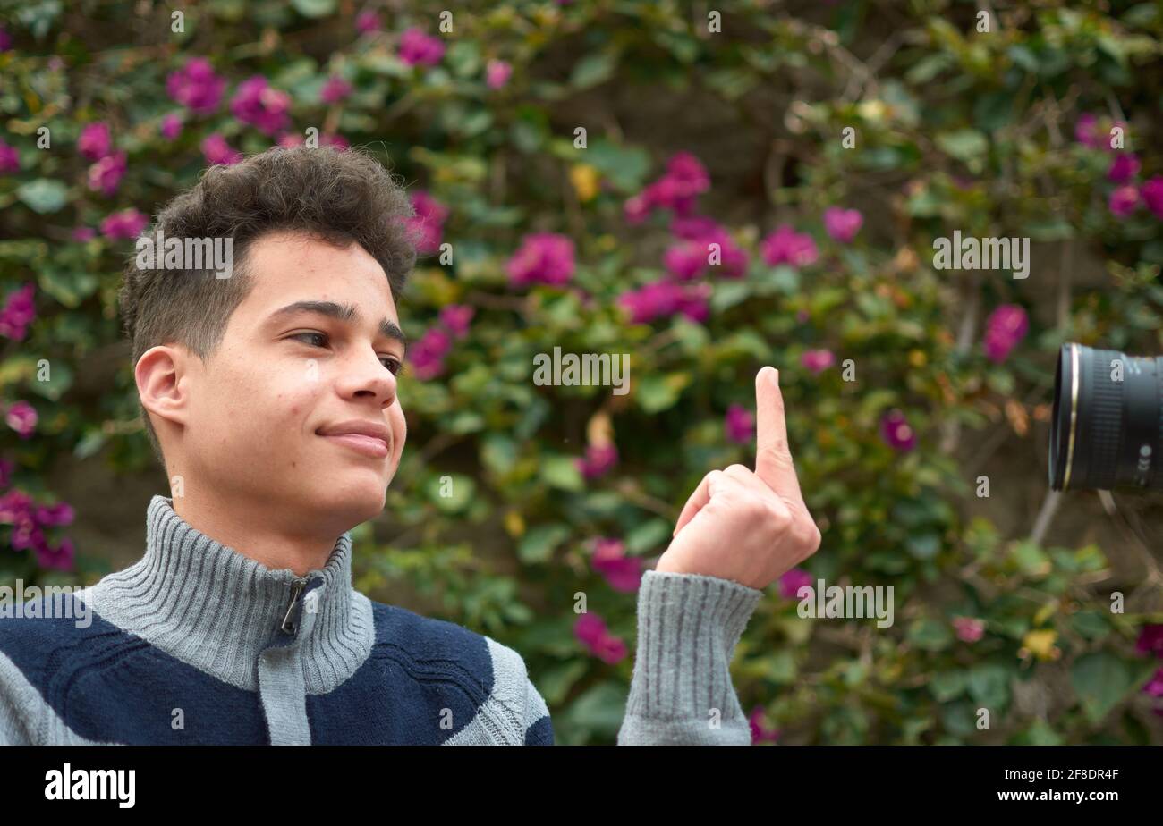 Portrait of a happy Hispanic male showing a middle finger in the park ...