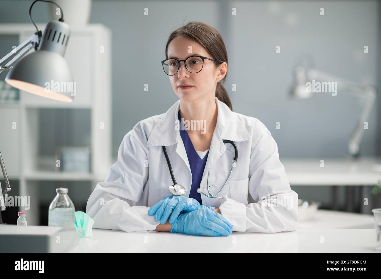 A young female internist is sitting at a desk in her spacious, bright ...