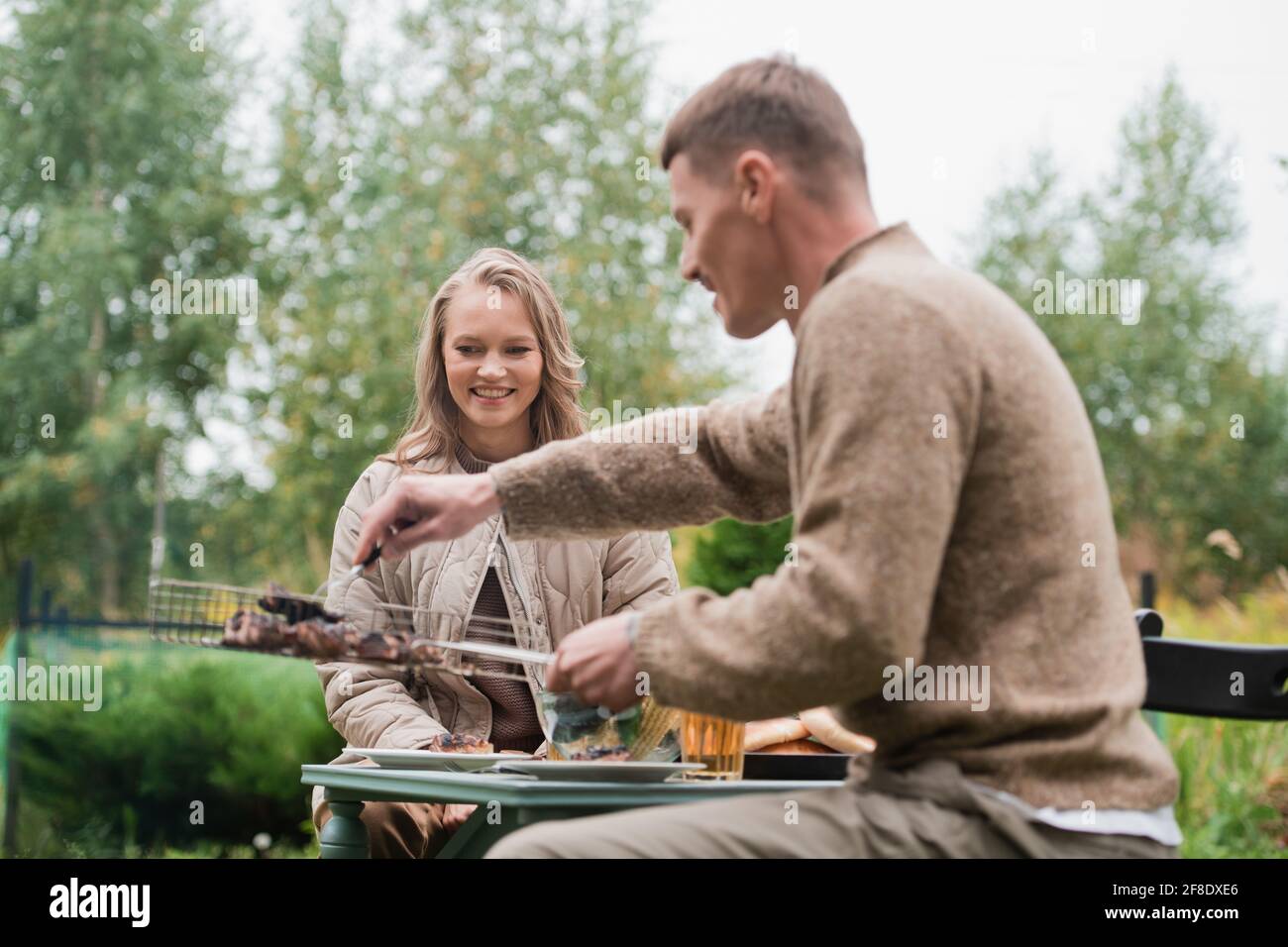 A young man is courting his fiancee. He puts chunks of grilled meat ...
