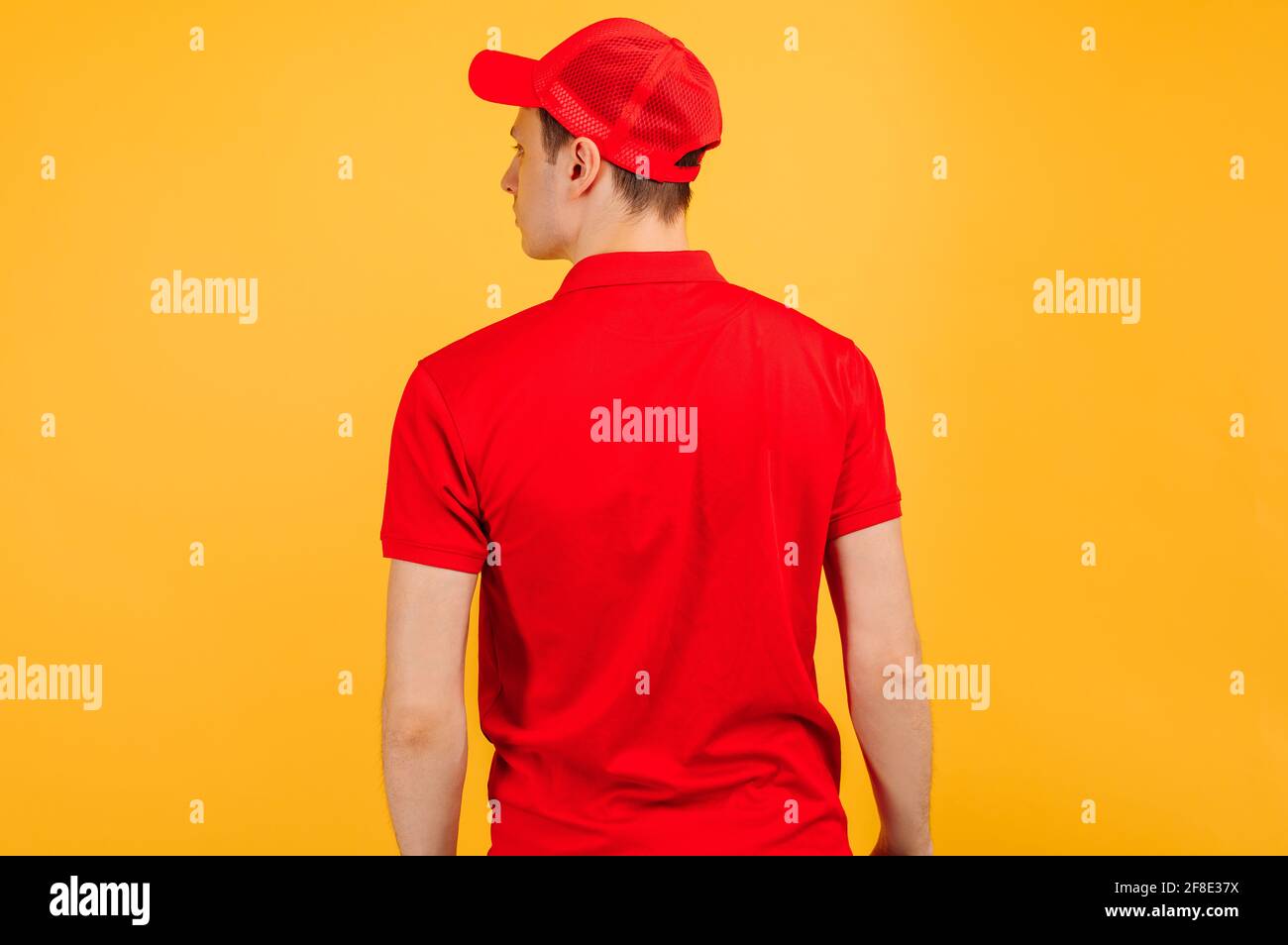 Rear view, courier wearing red uniform posing on yellow studio ...