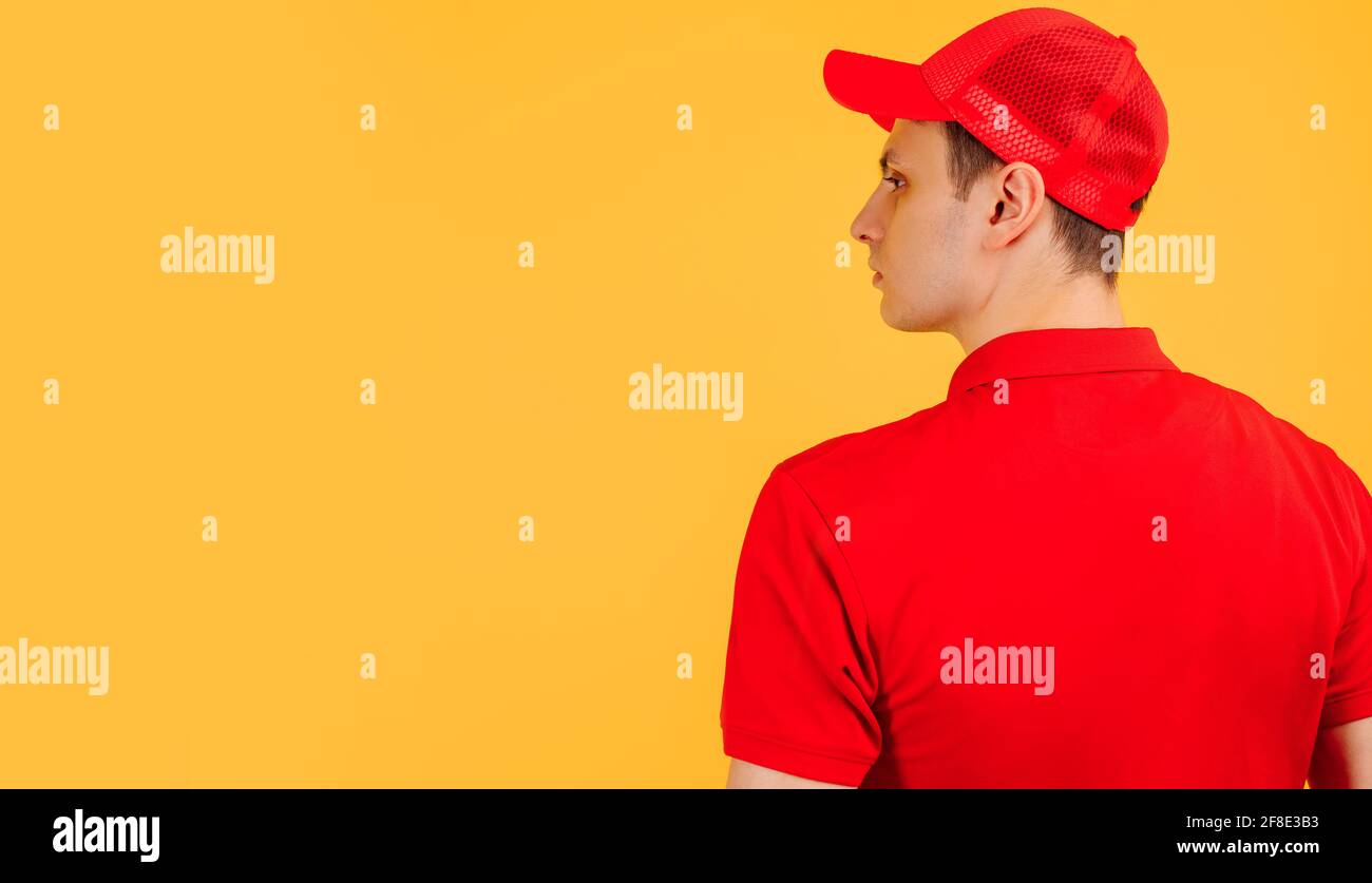 Rear view, courier wearing red uniform posing on yellow studio ...