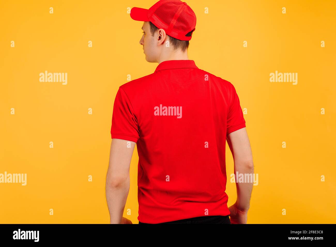 Rear view, courier wearing red uniform posing on yellow studio ...